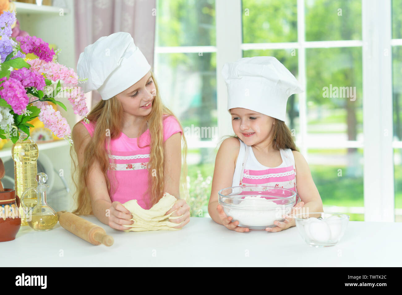Cute girls in chefs hats making dough in the kitchen at home Stock ...
