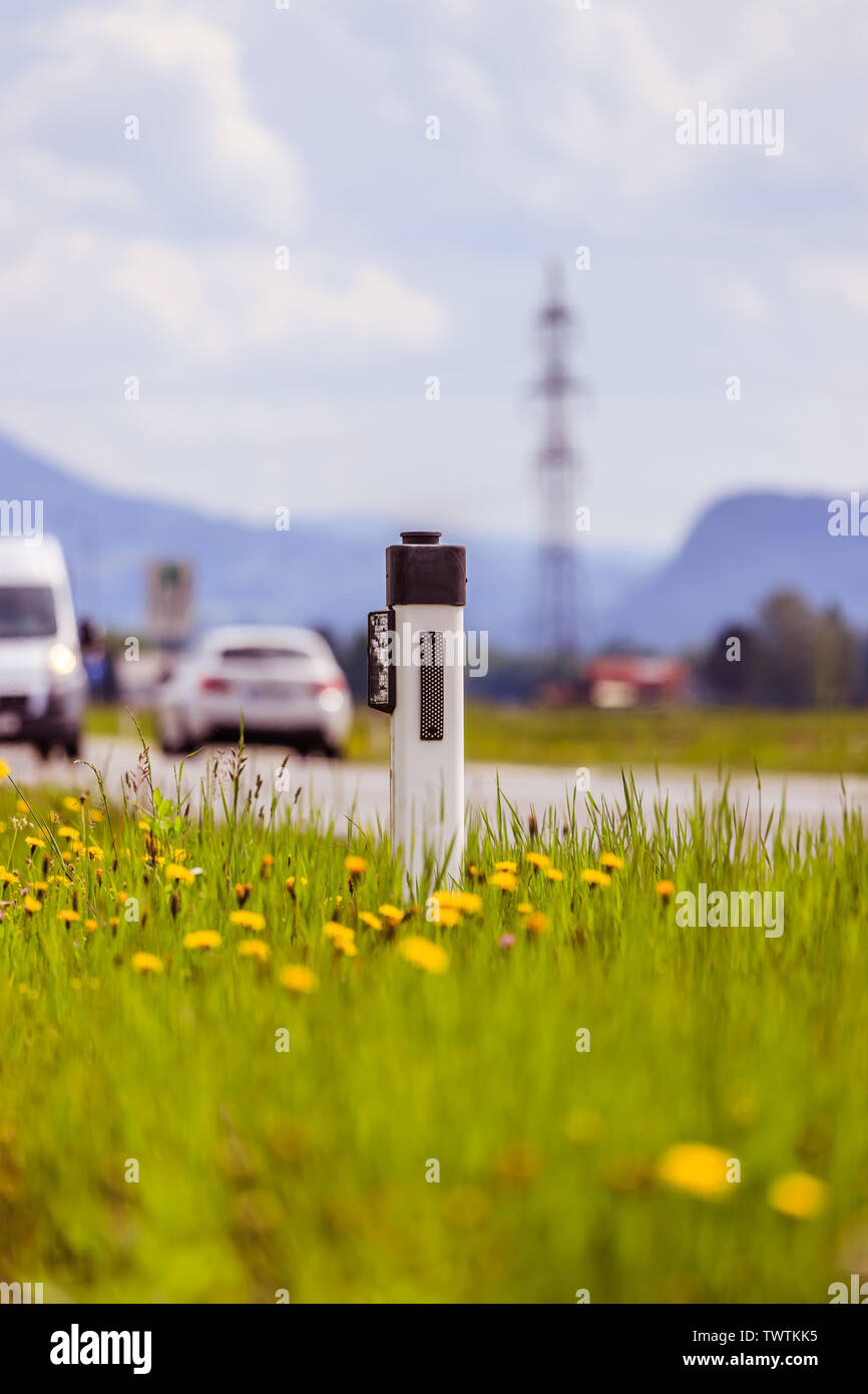 Reflector post and cars at an idyllic asphalted road in summer, flowers ...