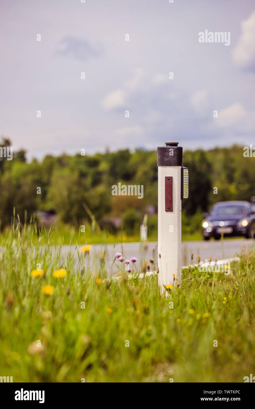 Reflector post and cars at an idyllic asphalted road in summer, flowers ...