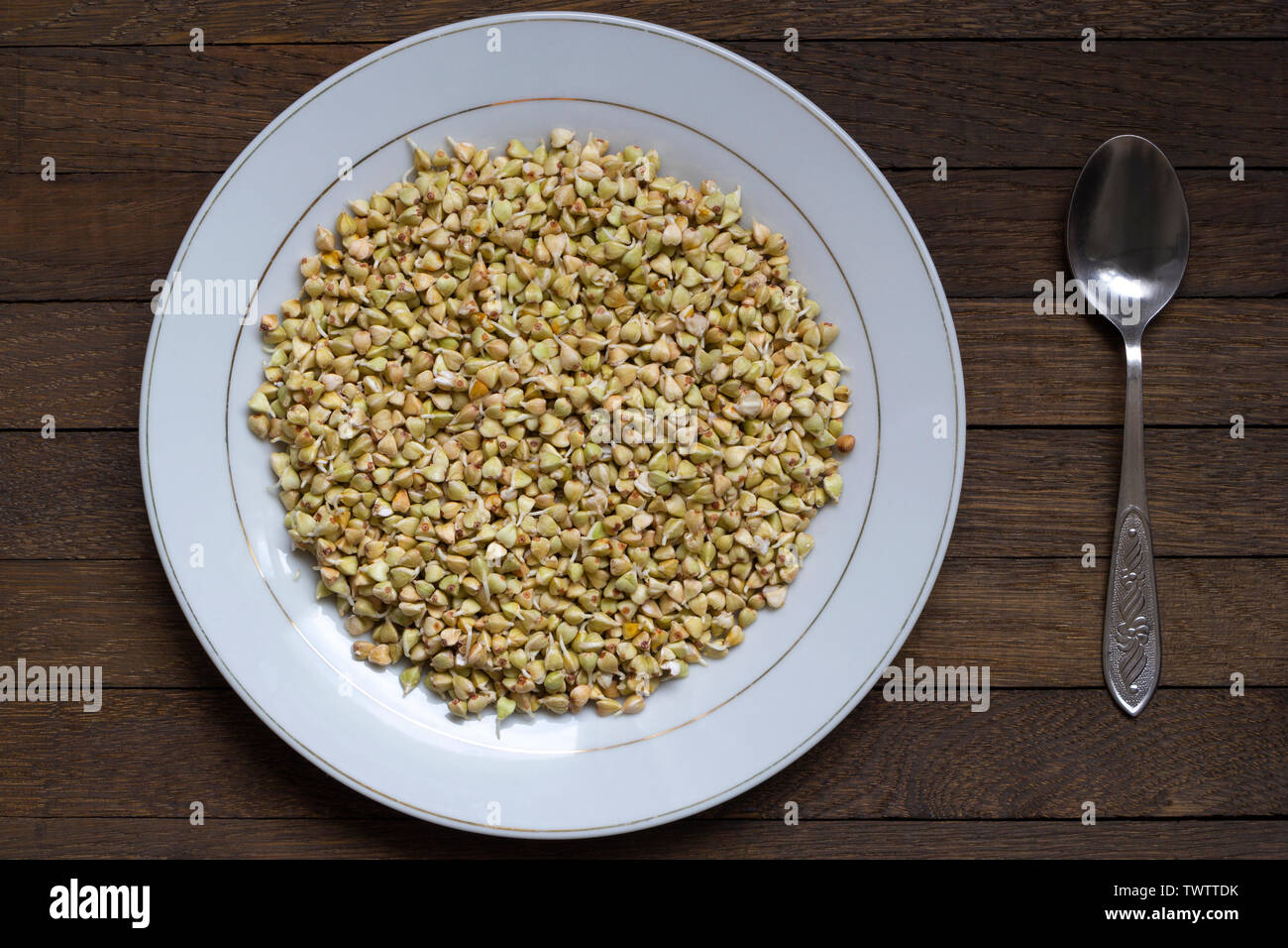 Sprouted buckwheat on white plate with spoon on brown wooden table. Top ...