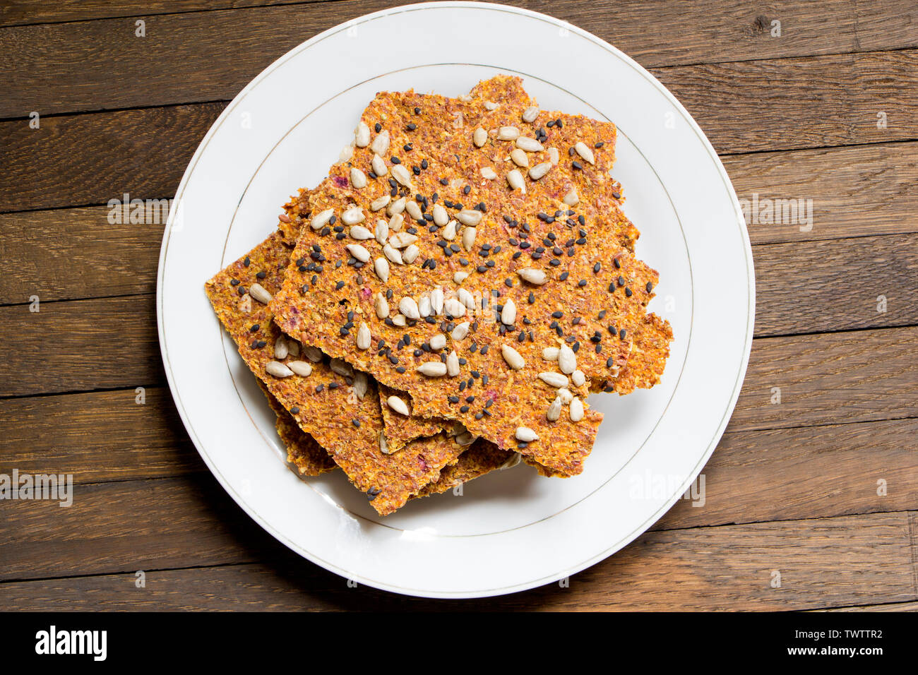 Dehydrated raw vegan breads on white plate on brown wooden table. Top ...