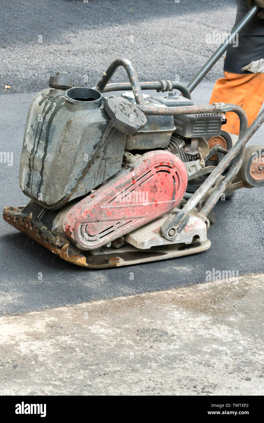 Road workers compact the asphalt with a vibrating rammer on the road ...