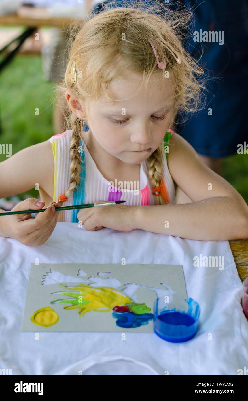 beautiful blond girl painting with brush into t-shirt with colorful ...