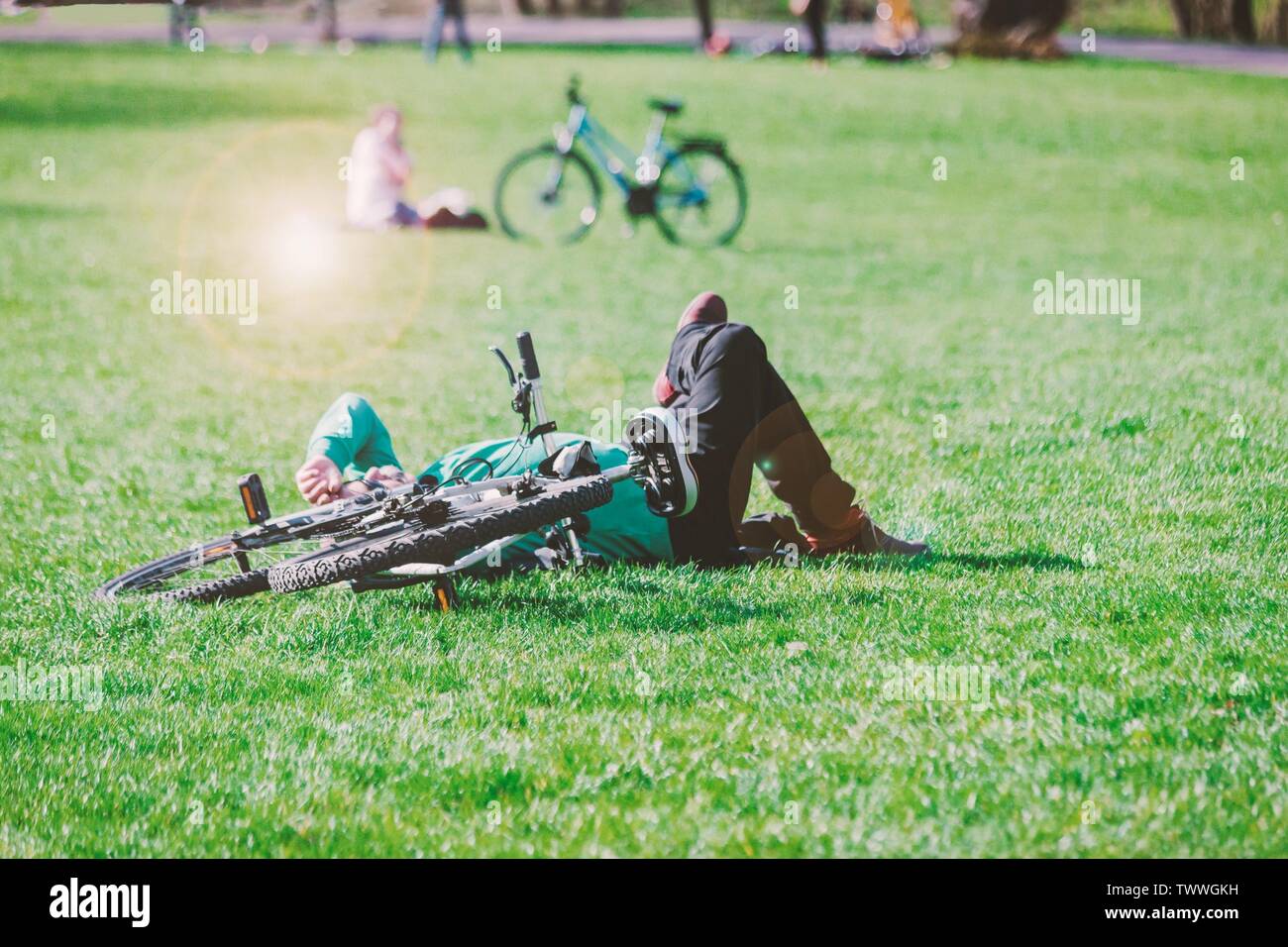A man with his bicycle lying on the green grass in the park. Sunny day ...