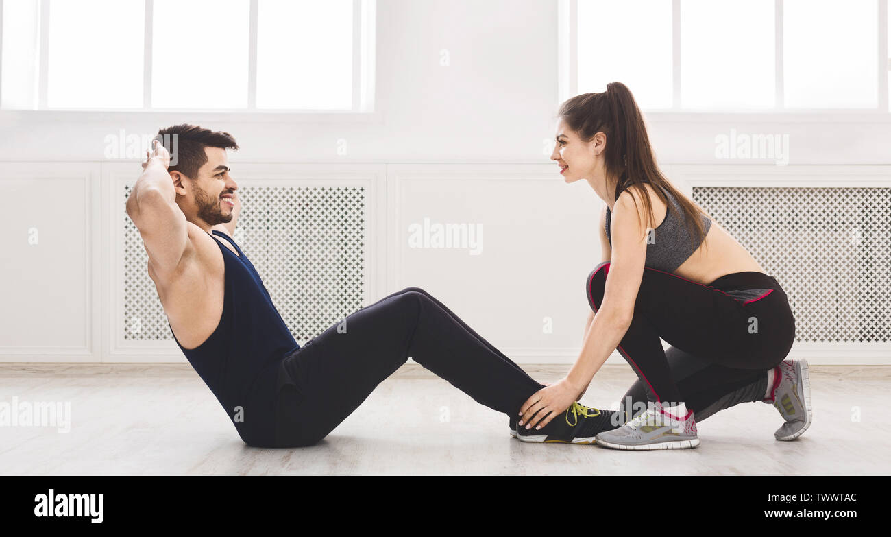 Athletic couple helping each other to sitting ups in studio Stock Photo ...
