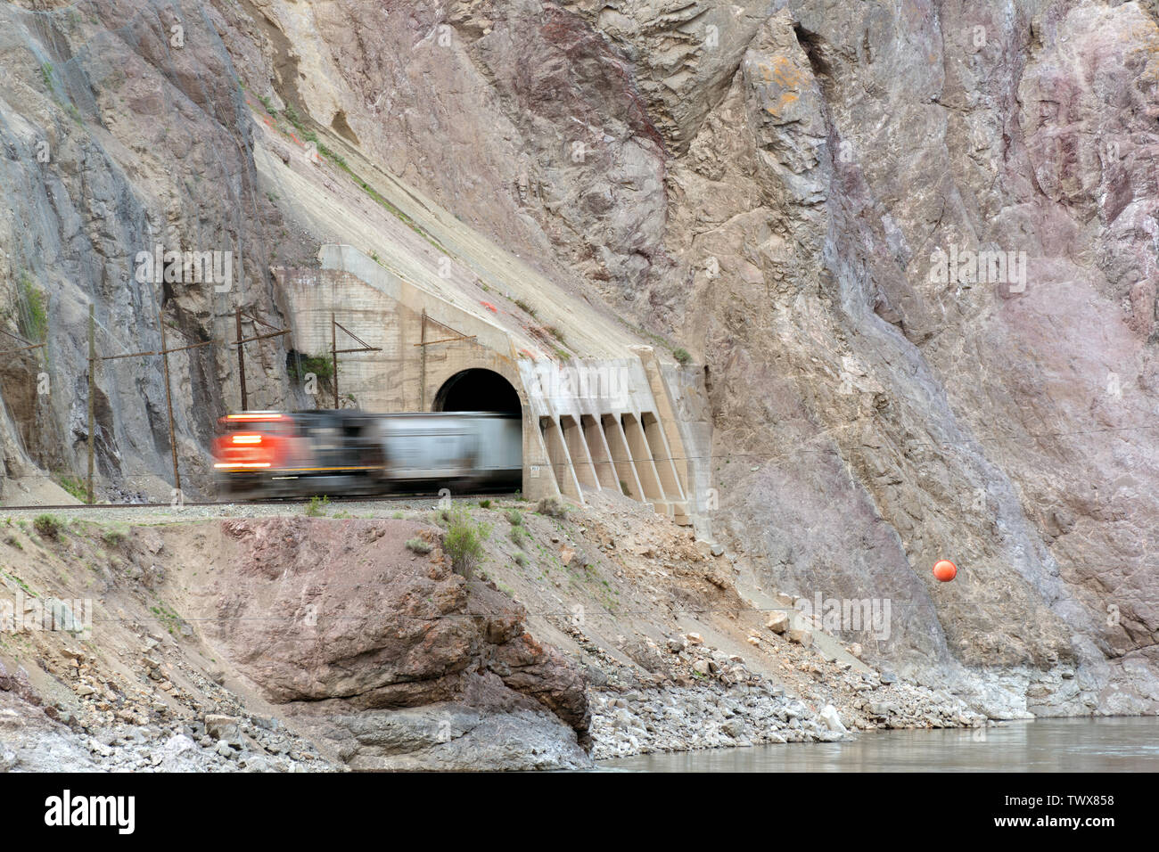 A train speeds out of a tunnel along the Thompson River in British ...