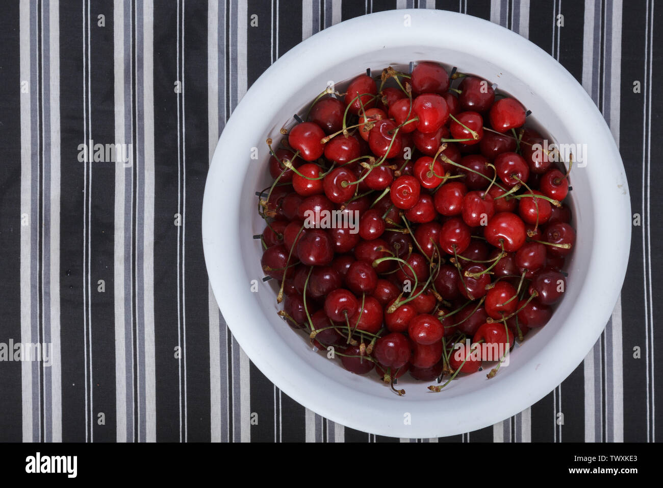 fresh sweet cherry in a white cup on a striped background top view ...