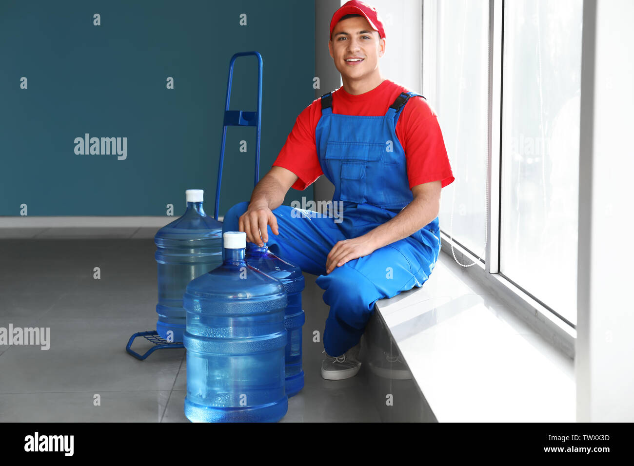 Delivery man with bottles of water sitting on window sill Stock Photo ...