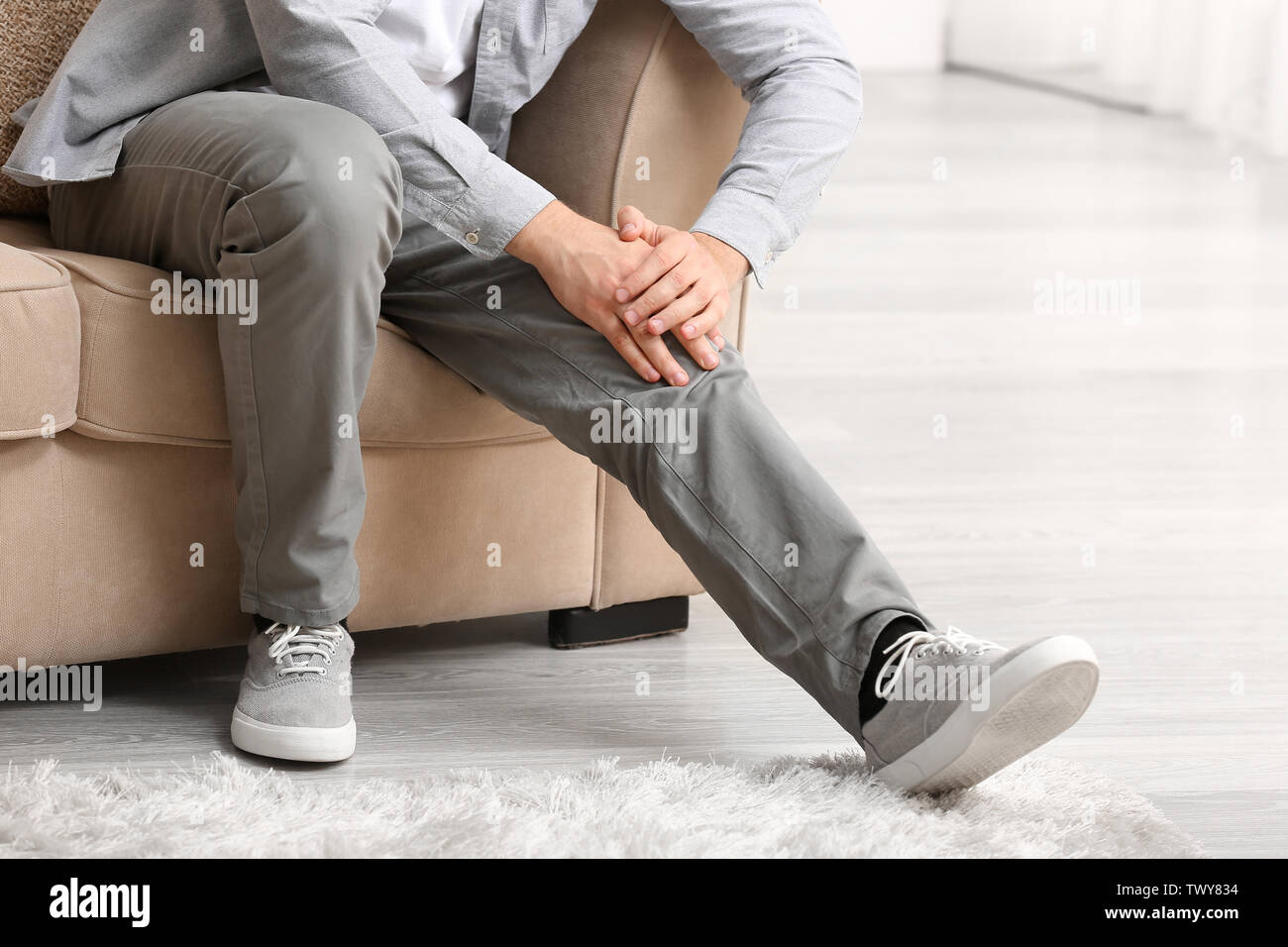 Young man suffering from pain in leg at home Stock Photo - Alamy