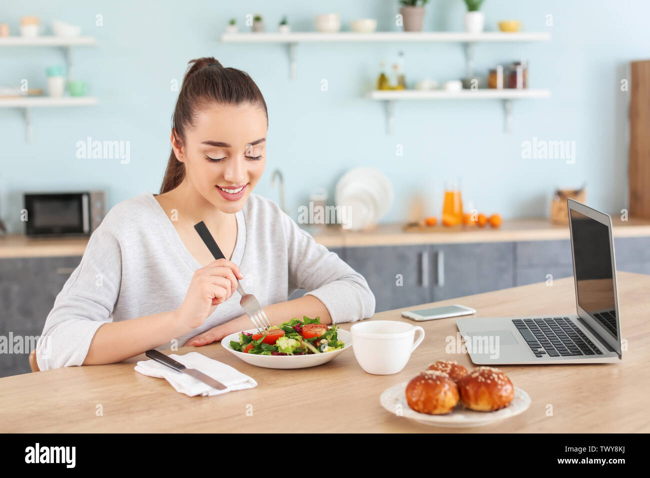 Beautiful woman eating at table in kitchen Stock Photo - Alamy