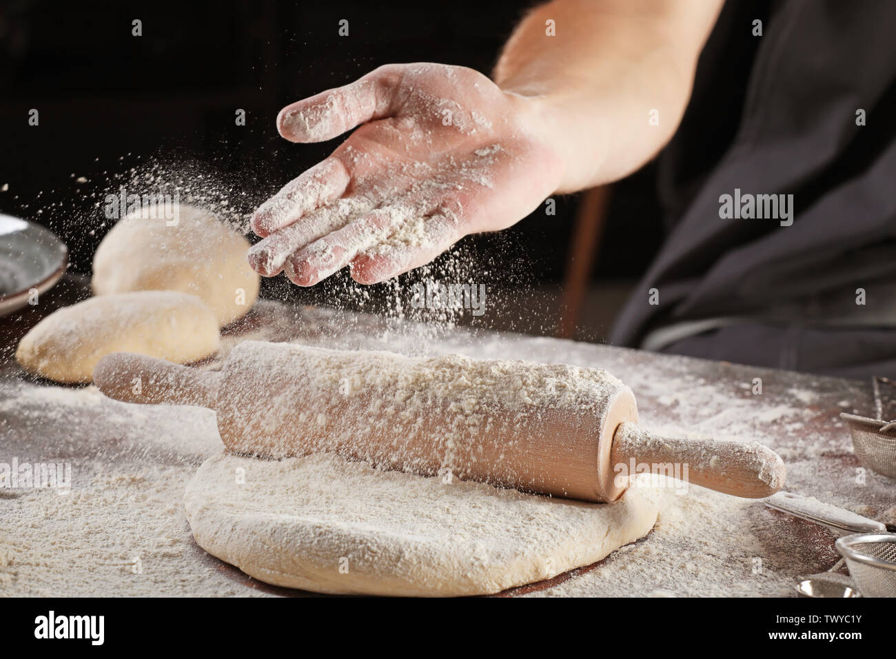 Man sprinkling dough with flour on table Stock Photo - Alamy