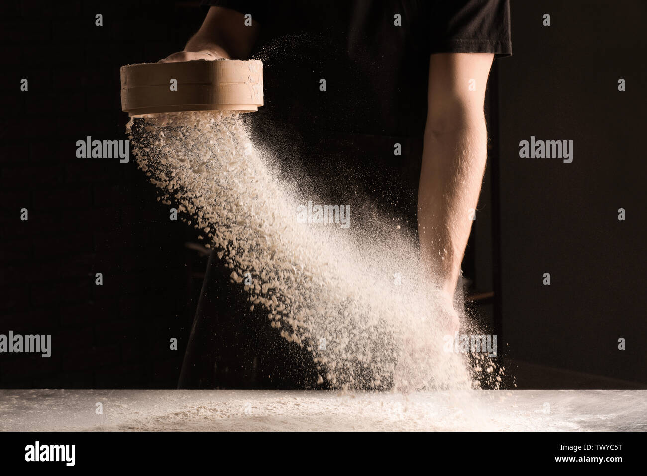 Man sieving flour on dark background Stock Photo - Alamy
