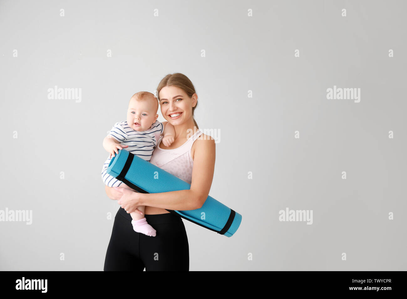 Sporty mother with cute little baby on light background Stock Photo - Alamy