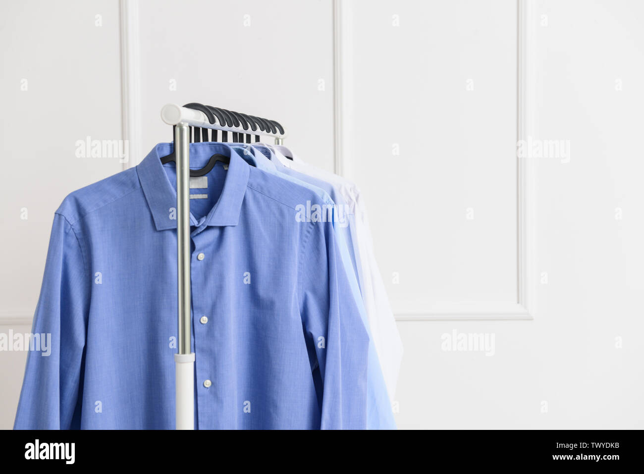 Rack with clothes after dry-cleaning near white wall Stock Photo - Alamy