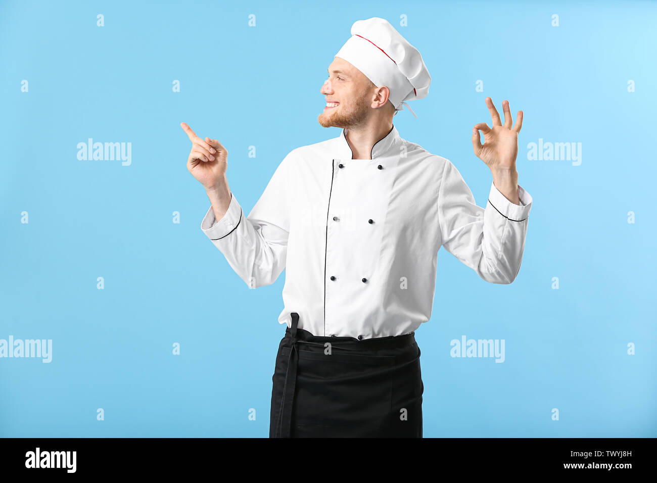 Handsome male chef pointing at something on color background Stock ...