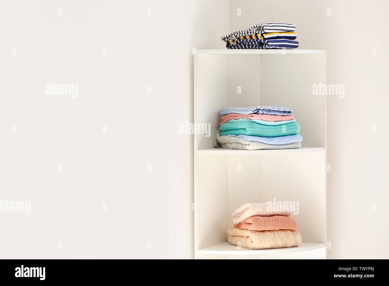 Rack with stacks of clean clothes near white wall Stock Photo - Alamy
