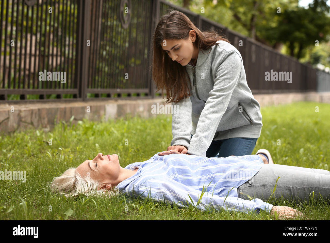 Female passer-by doing CPR on unconscious mature woman outdoors Stock ...