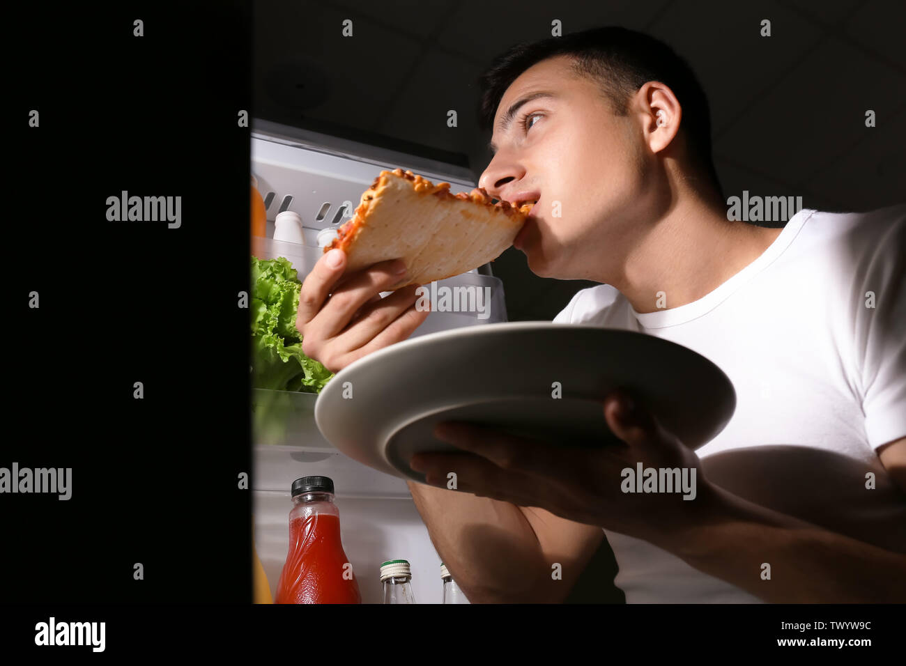 Young man eating pizza near refrigerator at night Stock Photo - Alamy