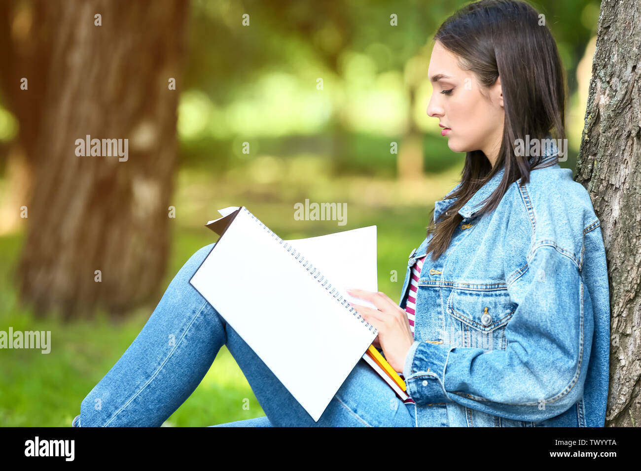 Beautiful female student sitting under tree in park Stock Photo - Alamy