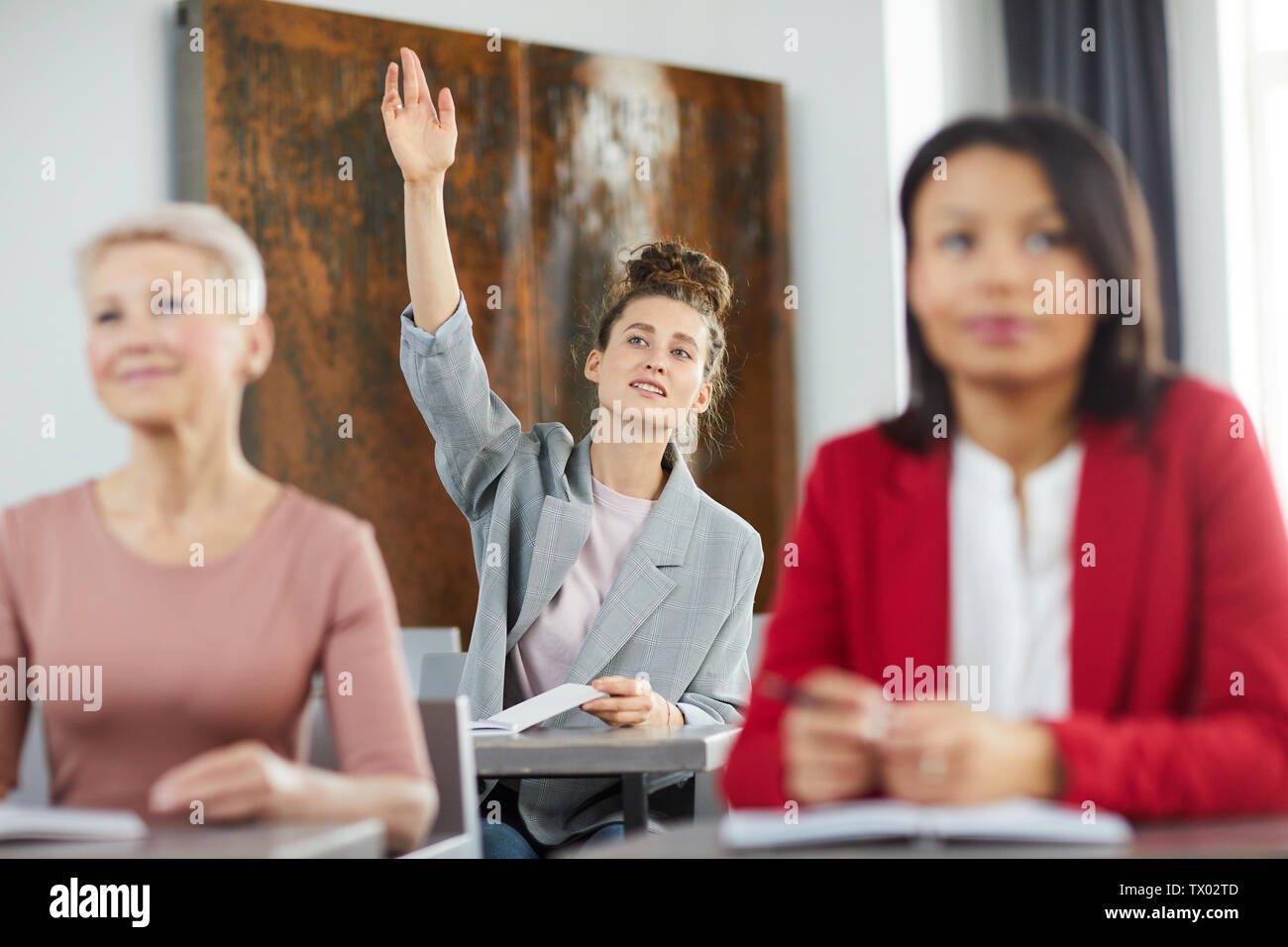 Portrait of contemporary young woman raising hand in class while ...