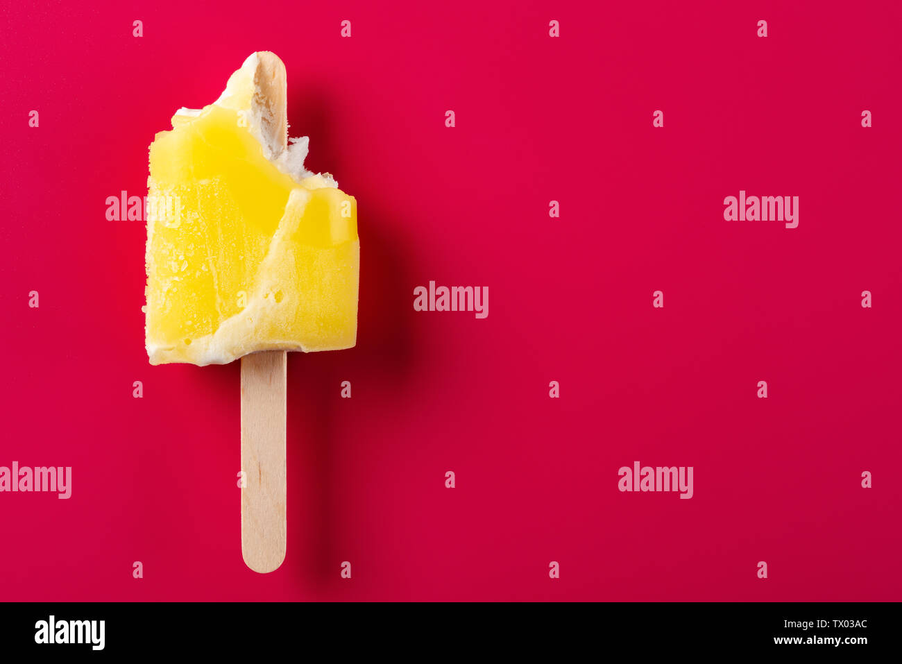 yellow popsicle with a couple of bites on a red background Stock Photo ...