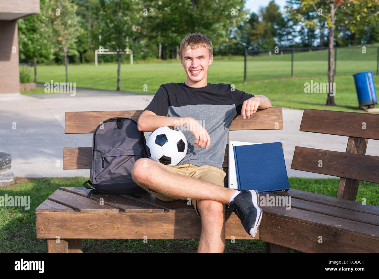 Happy teenager sitting on a bench with a soccer ball and his school ...