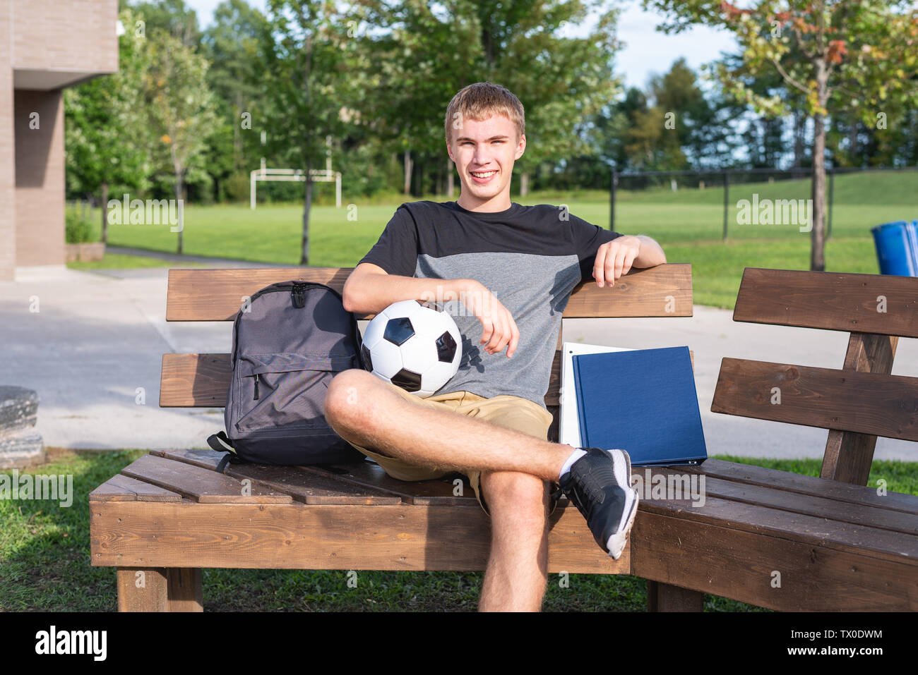 Happy teenager sitting on a bench with a soccer ball and his school ...