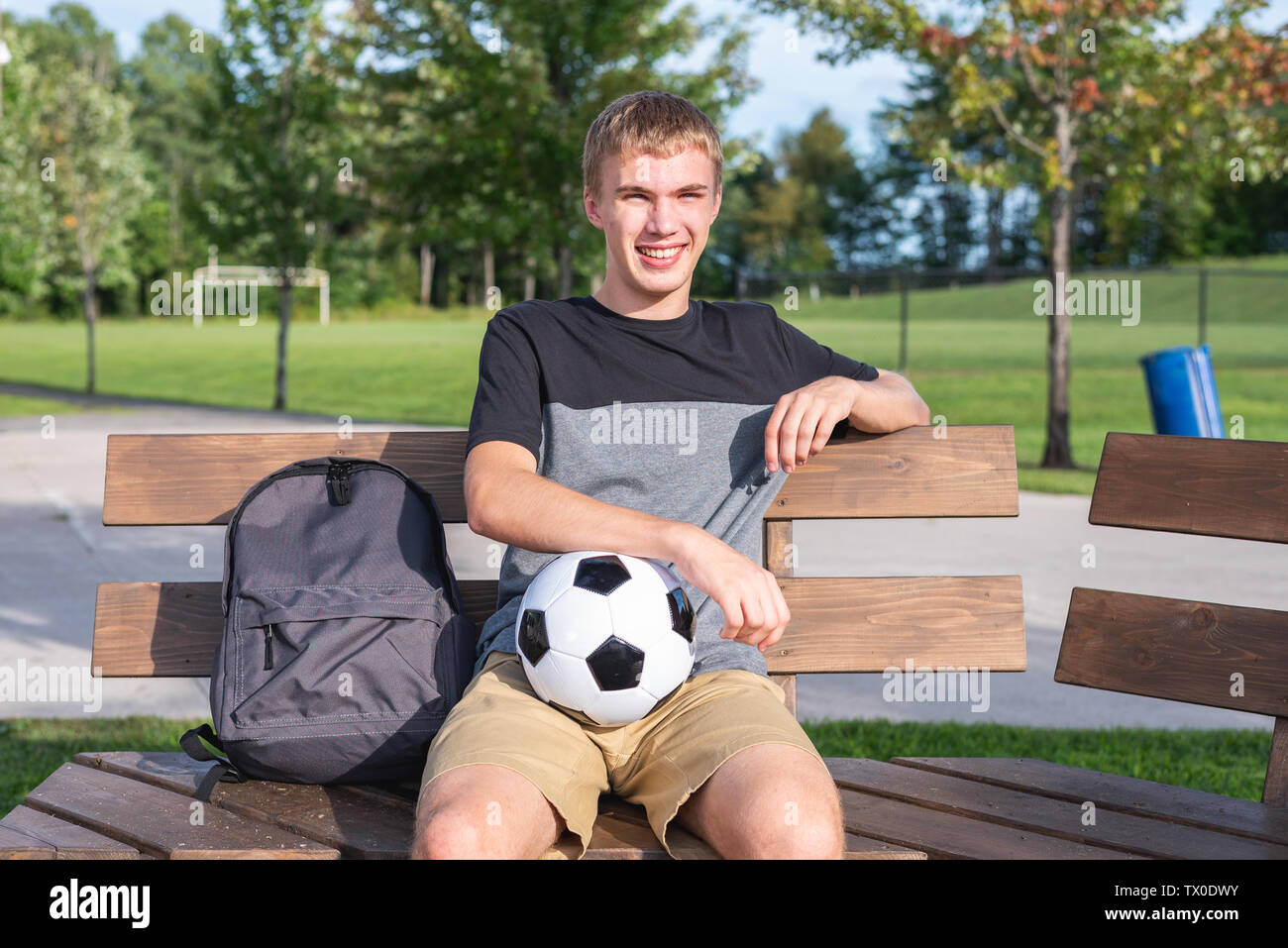 Happy teenager sitting on a bench with a soccer ball and his school ...