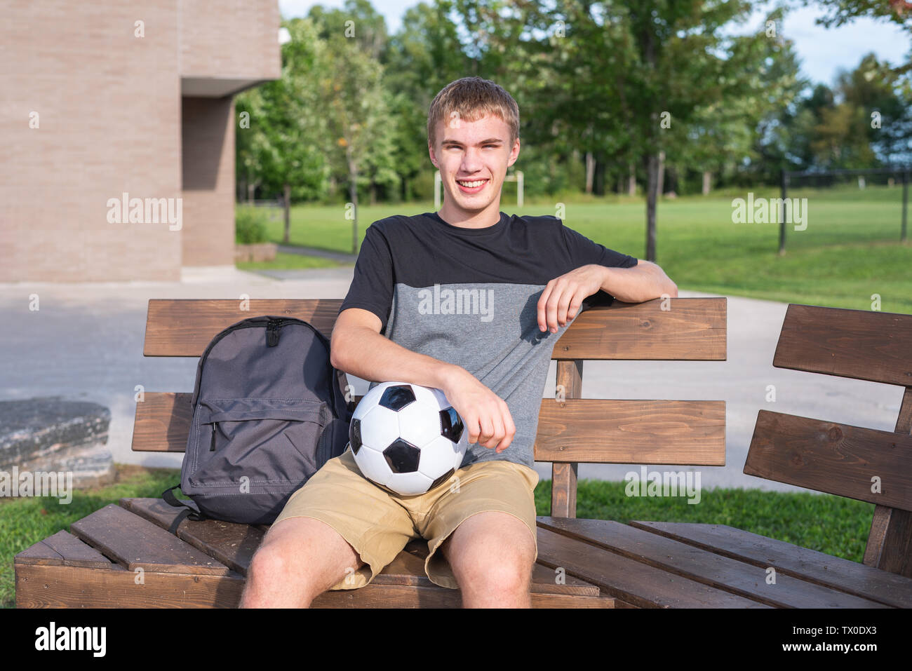 Happy teenager sitting on a bench with a soccer ball and his school ...