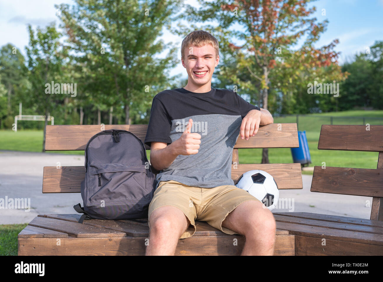 Happy teenager sitting on a bench with a soccer ball and his school ...