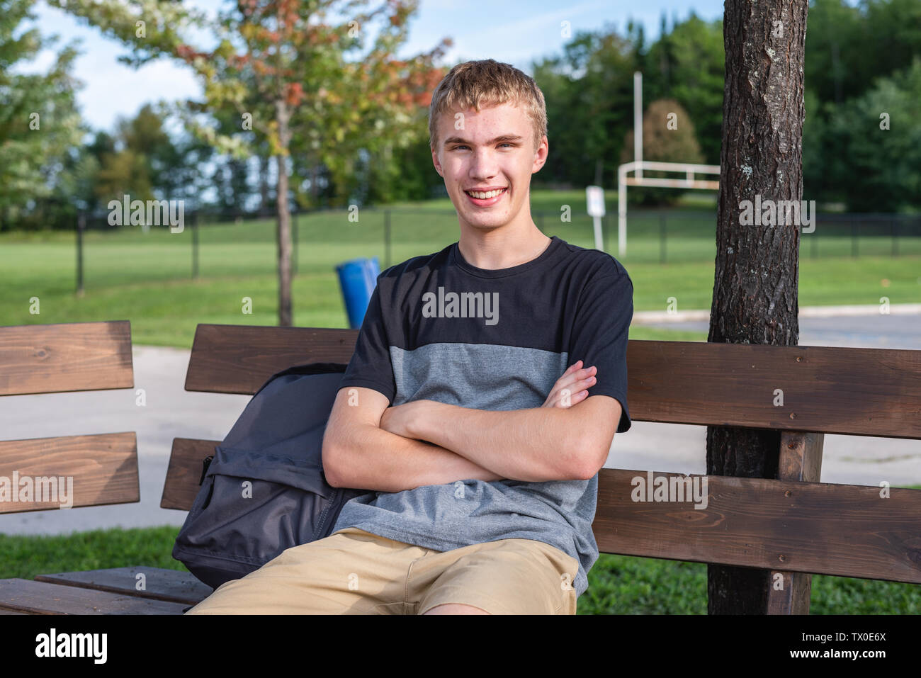 Happy teenager sitting on wooden bench that is next to a soccer ...
