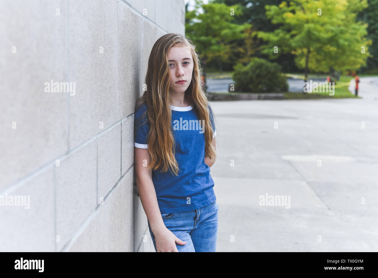 Sad teenage girl leaning against brick wall of a school Stock Photo - Alamy