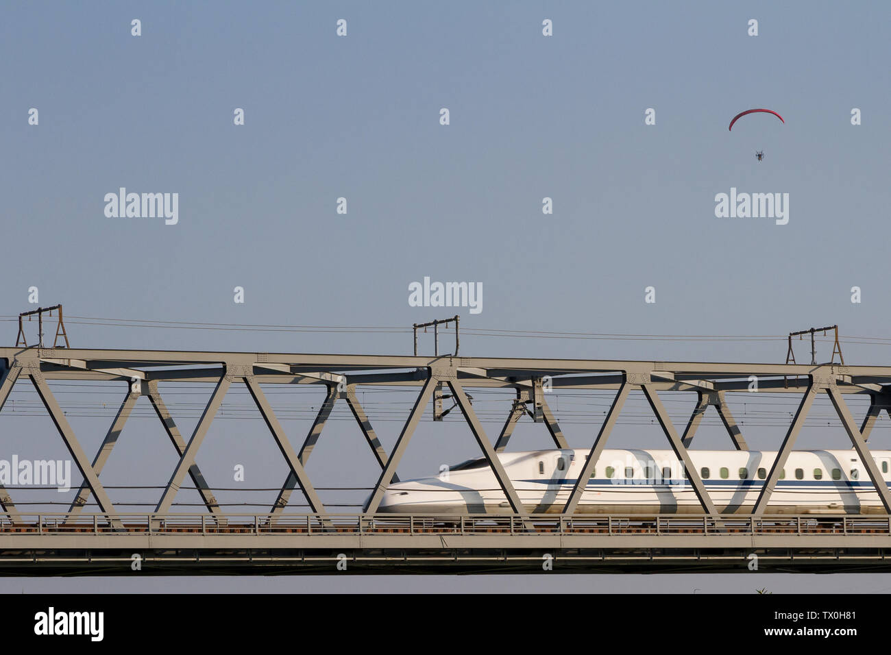 A parapenter flies over a bridge as an N700 series shinkansen (bullet ...