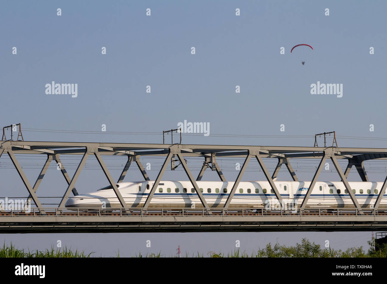 A parapenter flies over a bridge as an N700 series shinkansen (bullet ...