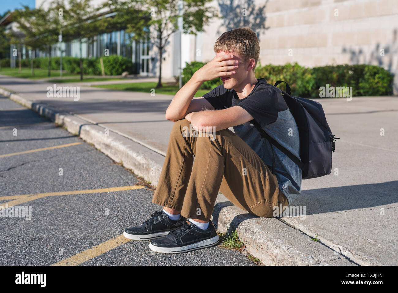 Upset teenager resting his head on his hand as he sits on the curb in ...