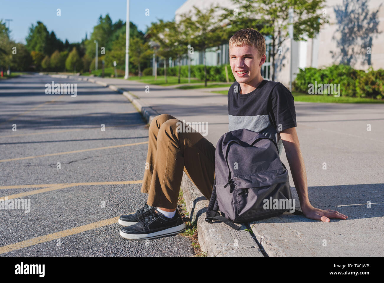 Happy teenager sitting on curb in front of high school Stock Photo - Alamy