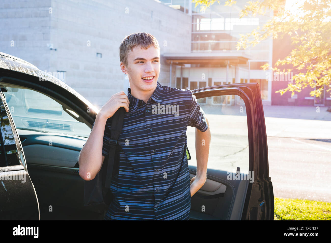 Happy teenager exiting his car and putting on his backpack as he ...