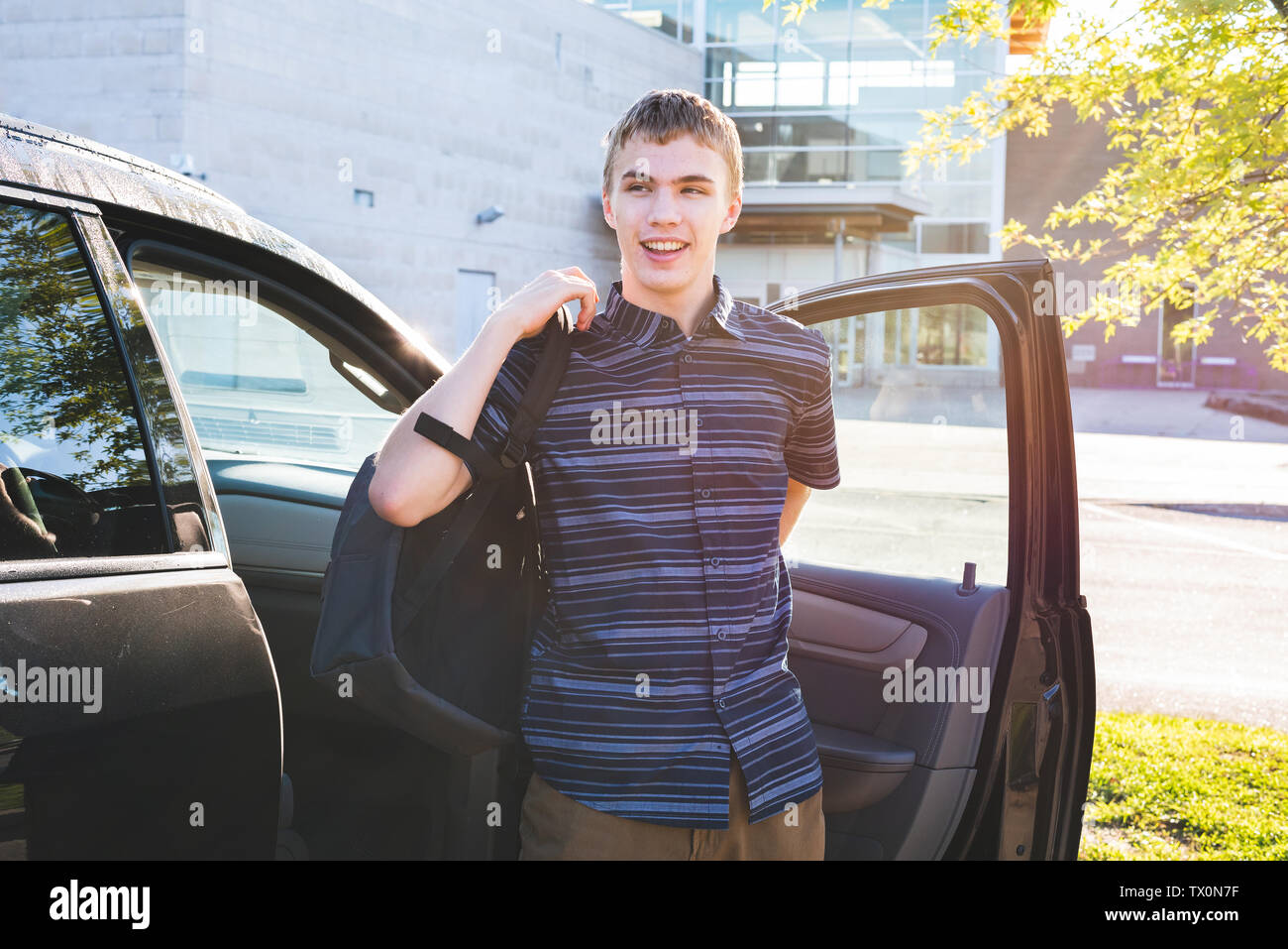 Happy teenager exiting his car and putting on his backpack as he ...