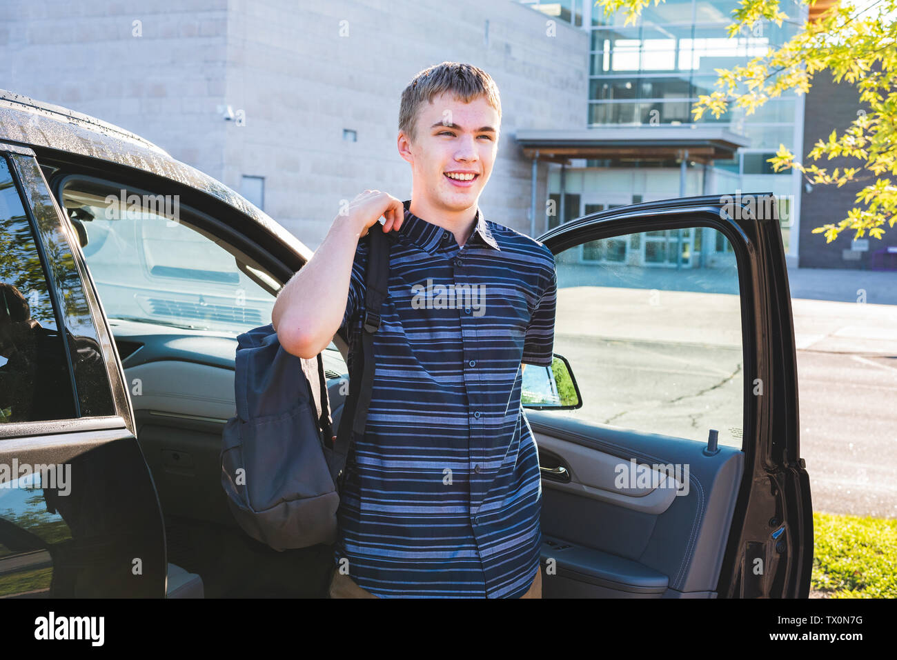 Happy teenager exiting his car and putting on his backpack as he ...