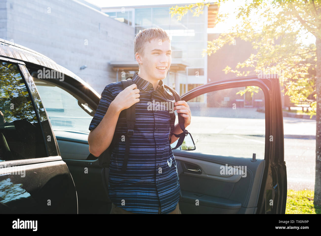 Happy teenager exiting his car and putting on his backpack as he ...
