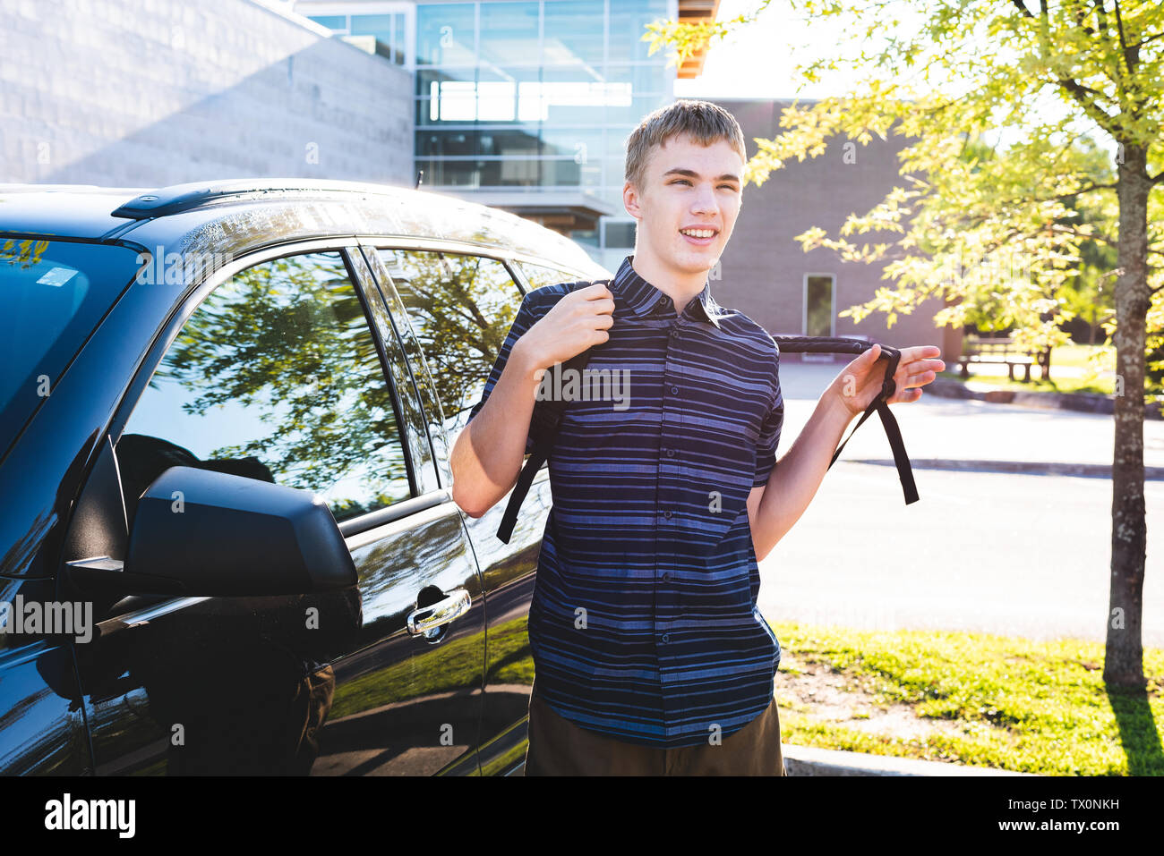 Teenager standing beside his car and putting on his backpack before ...