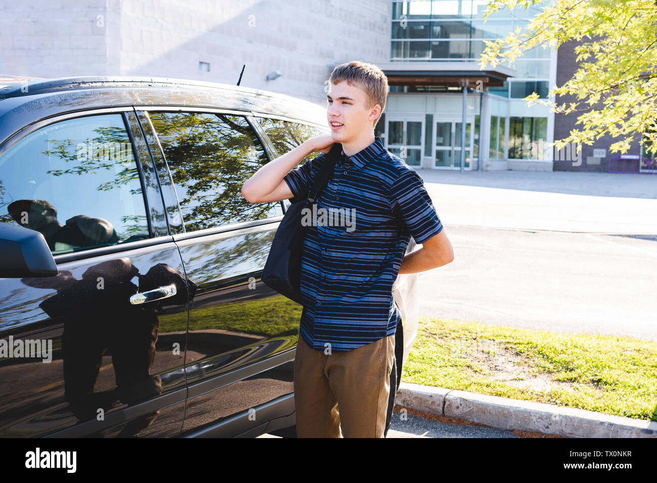 Teenager standing beside his car and putting on his backpack before ...