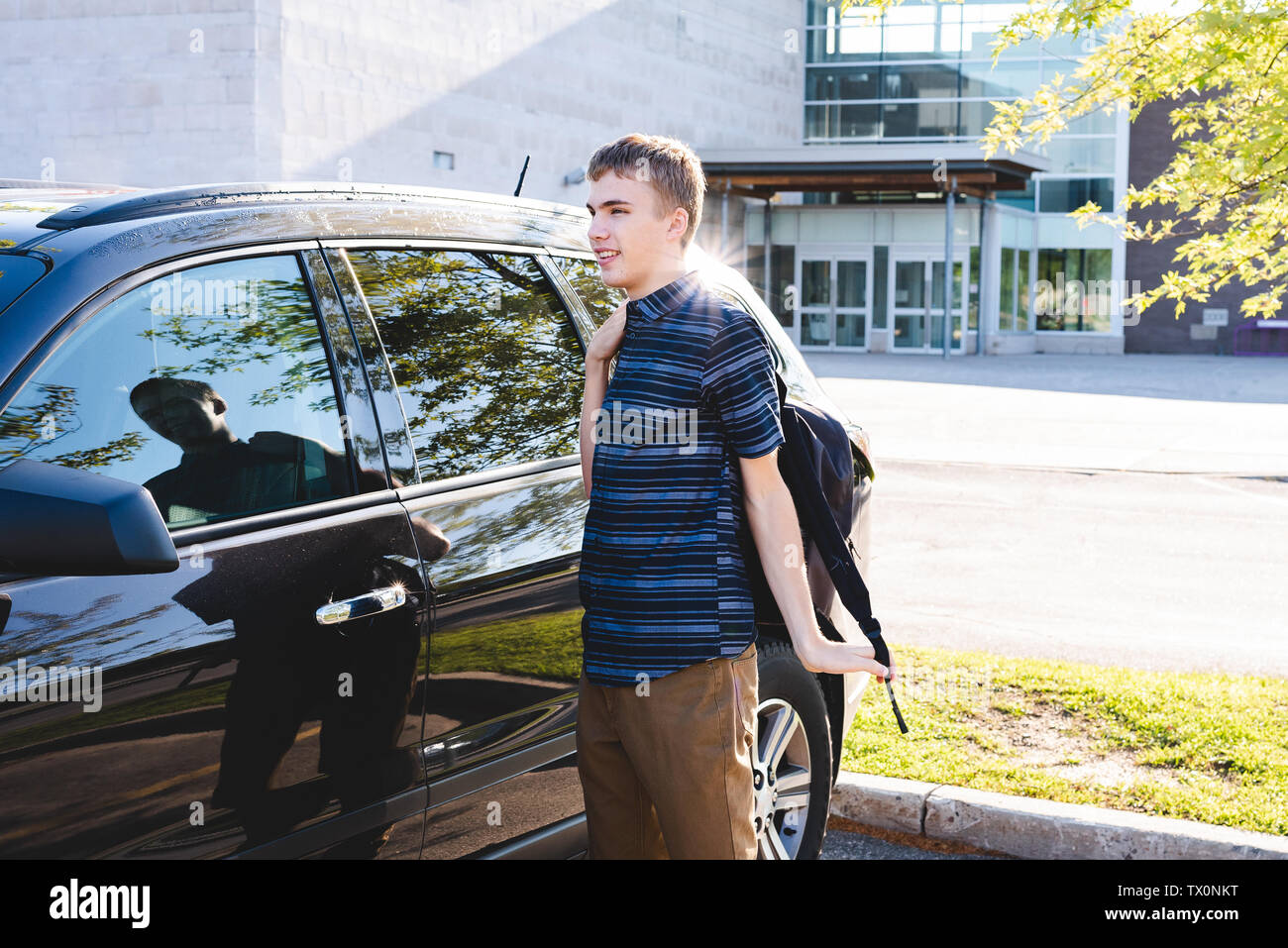 Teenager standing beside his car and putting on his backpack before ...