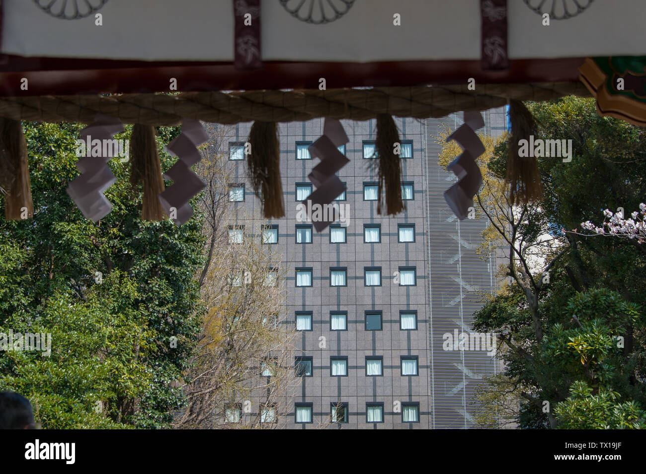 Paper Shide hang across entrance to a Shinto Shrine with view to a city ...