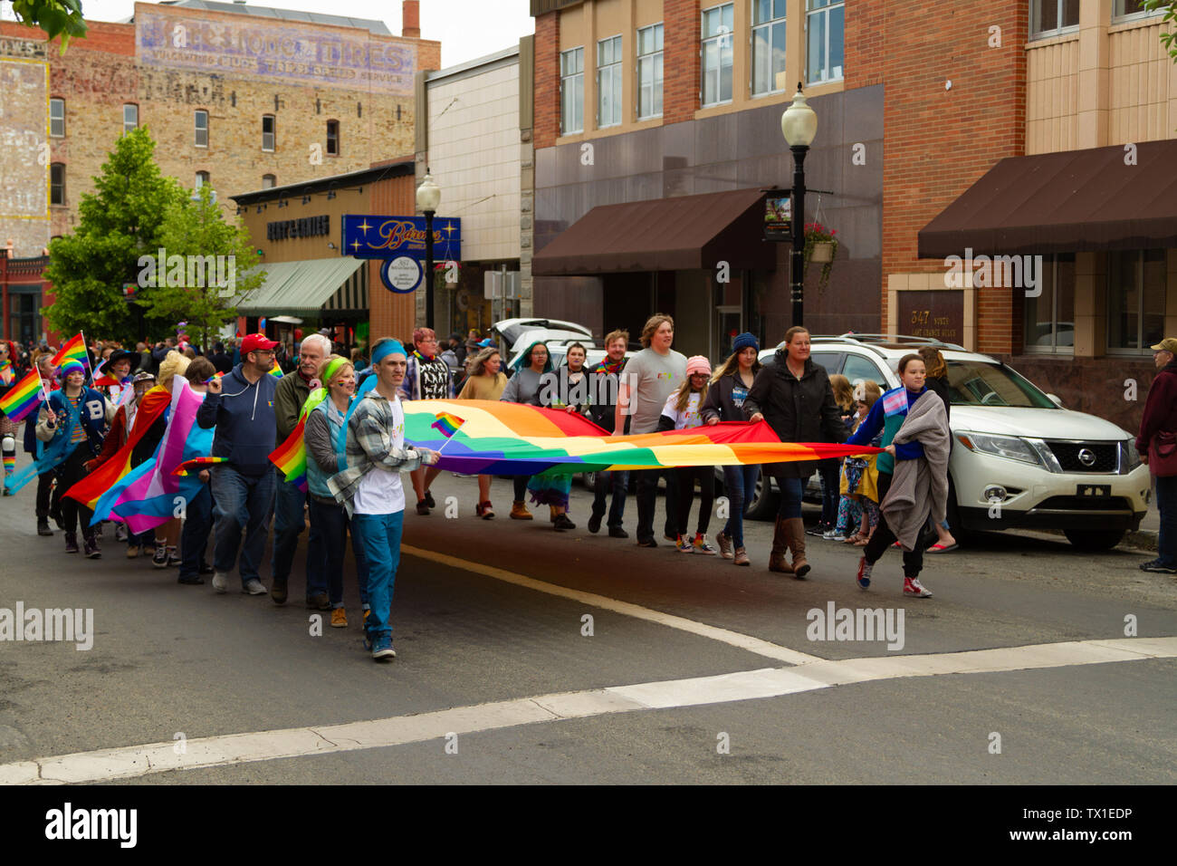 Large group of people, multiple ages, carrying a large rainbow flag in ...