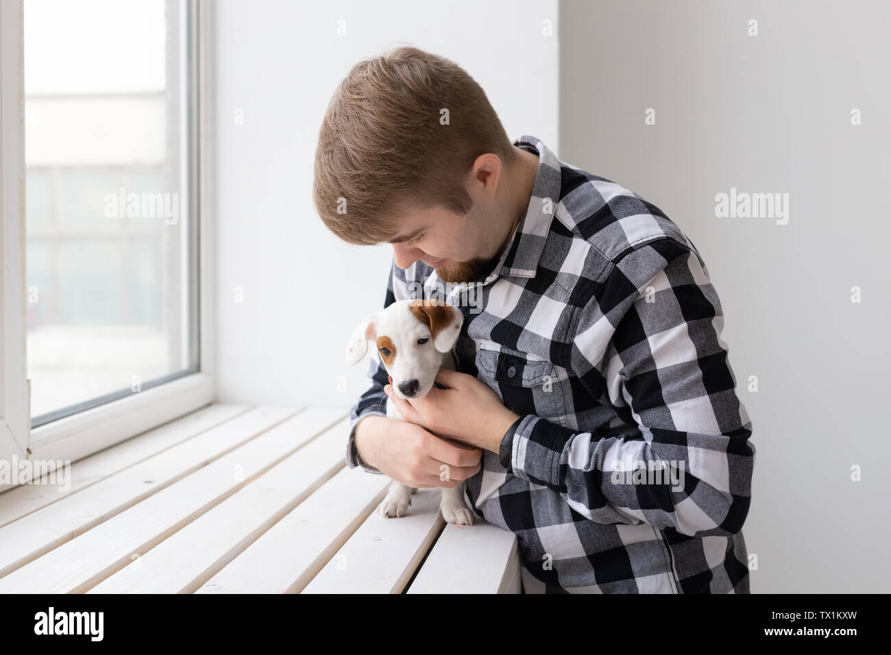 people, pets and animals concept - young man hugging puppy near window ...