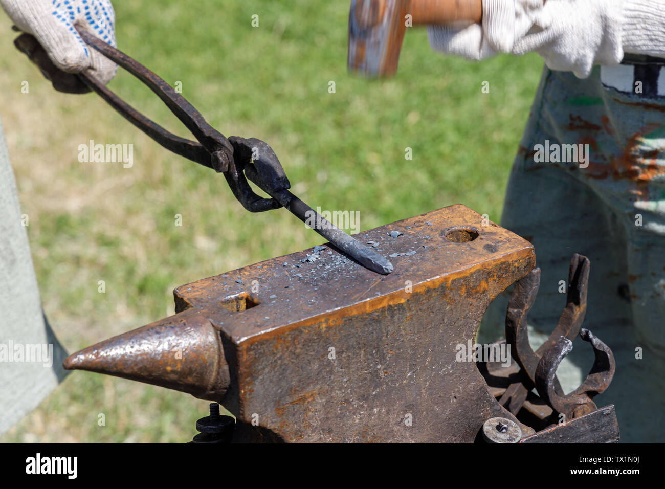 Blacksmith forges metal billet on the anvil against the background of ...