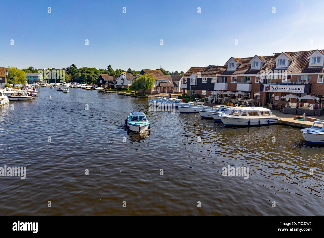 A small hire boat motoring up the River Bure towards the road bridge in ...