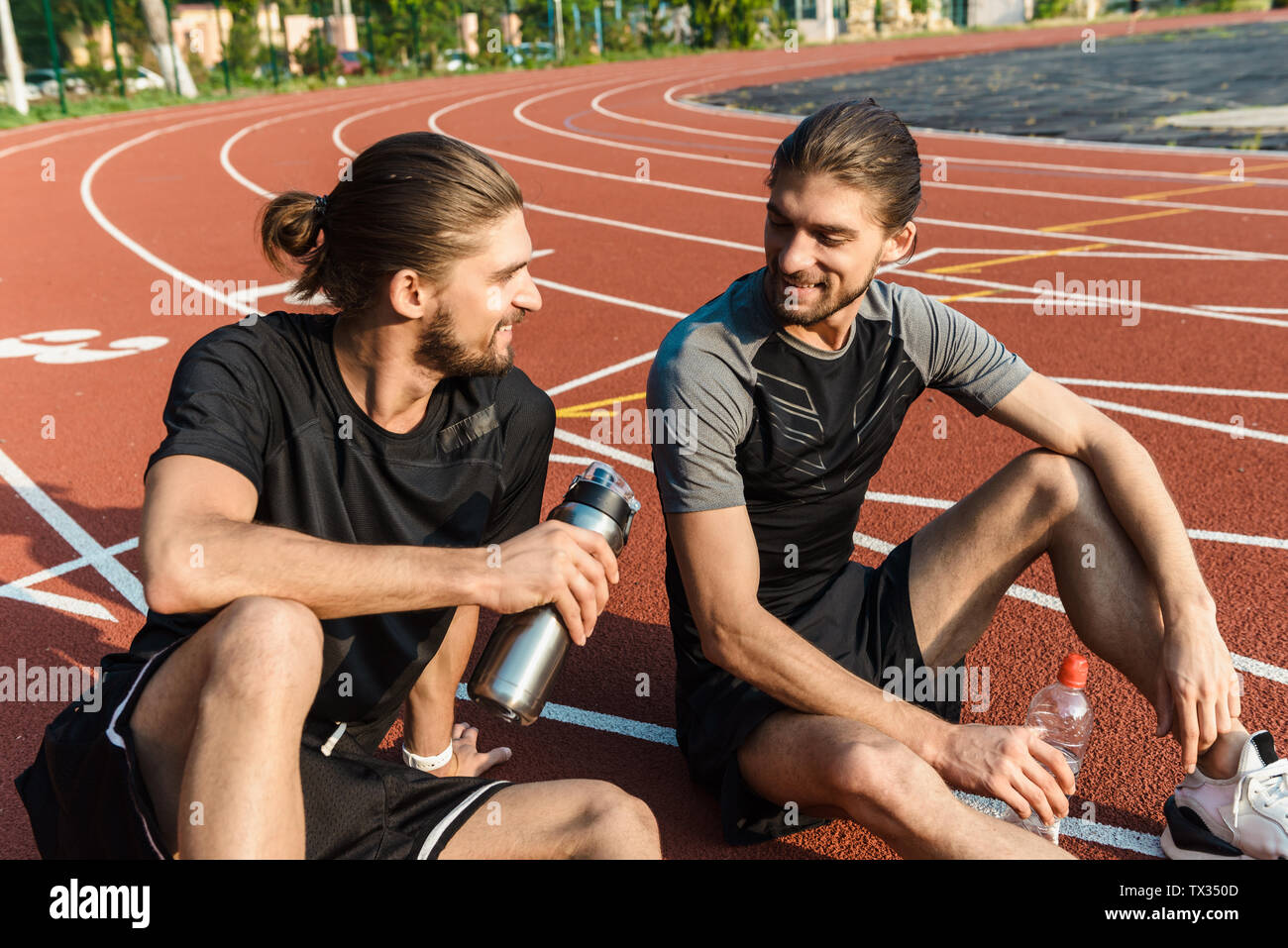 Two healthy fit twin brothers exercising outdoors, resting, drinking ...