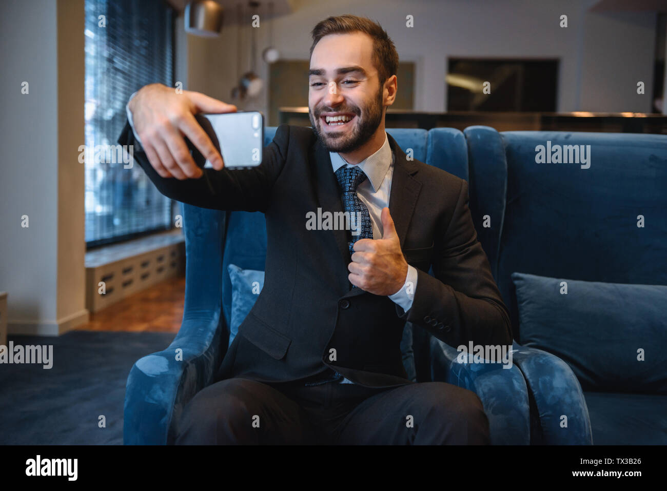 Handsome young excited businessman wearing suit sitting at the hotel ...